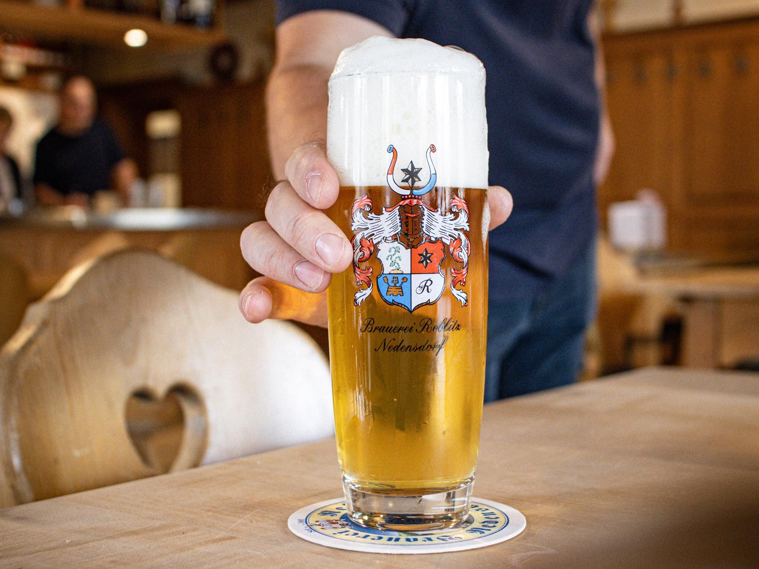 Uma cerveja em copo com um brasão na lateral, segurada por alguém.