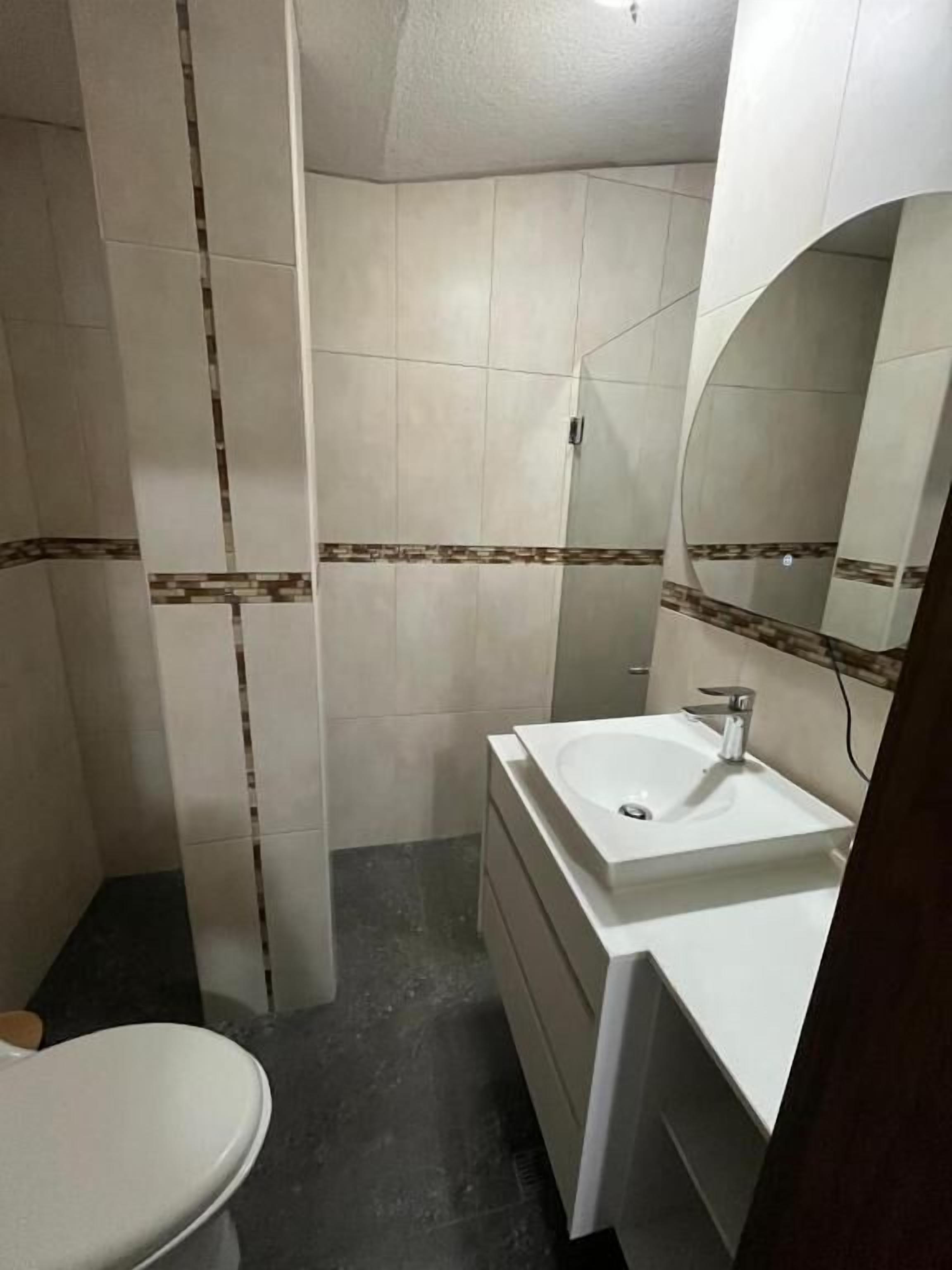 Um banheiro com vaso sanitário, pia, espelho e paredes revestidas de azulejos.