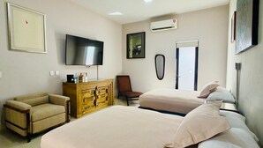 Quarto de hotel com duas camas, televisão, cômoda, uma cadeira e ar condicionado.