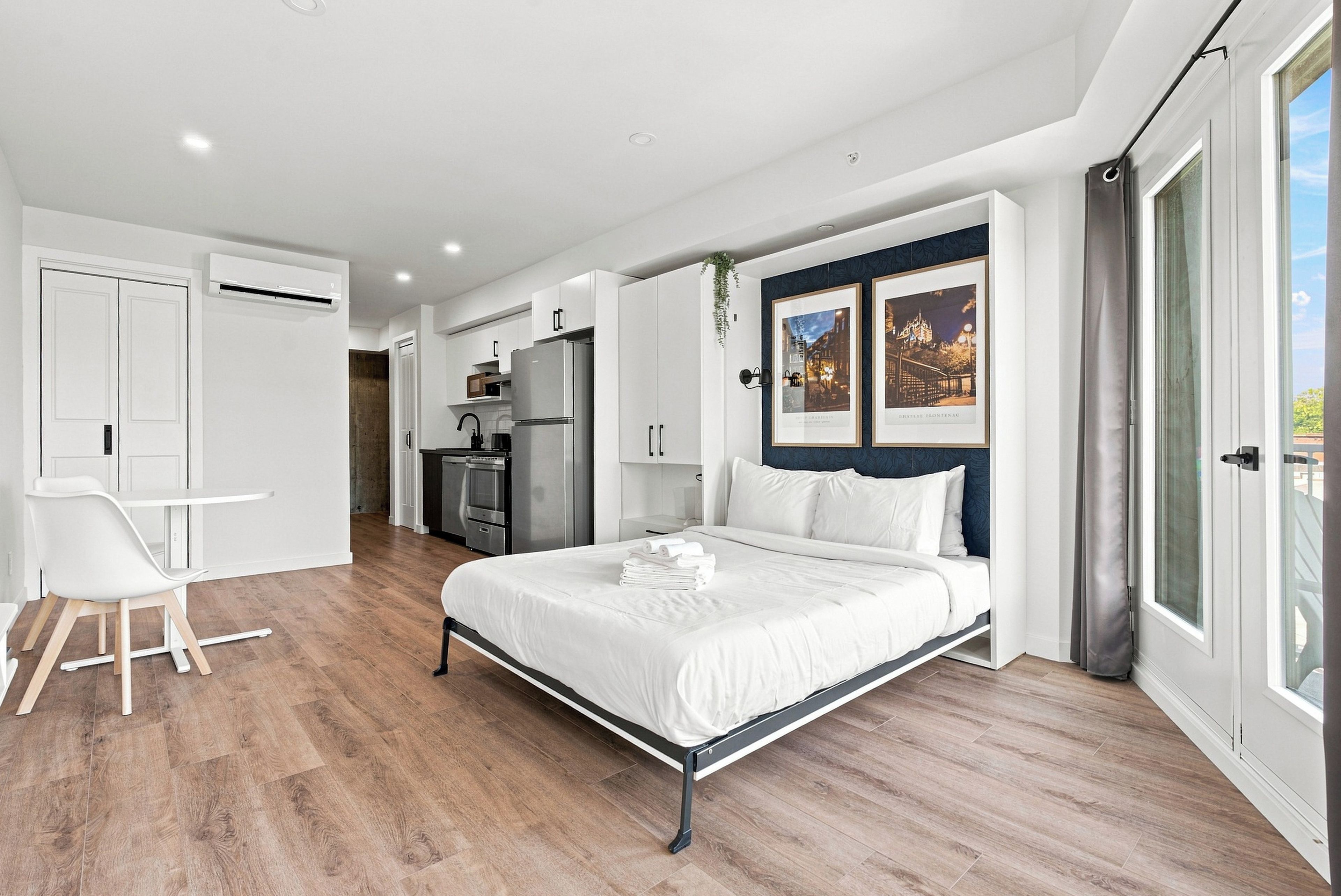 Quarto moderno com cama, escrivaninha e kitchenette.