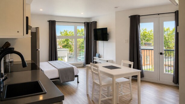 Quarto de hotel moderno com cama, escrivaninha, cadeira, TV e varanda com cortinas.