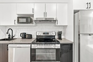 Cozinha moderna com armários brancos, micro-ondas, fogão, lava-louças e geladeira.
