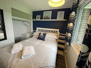 Cama bem arrumada com almofadas, mesa de cabeceira, radiador e janela com cortinas.