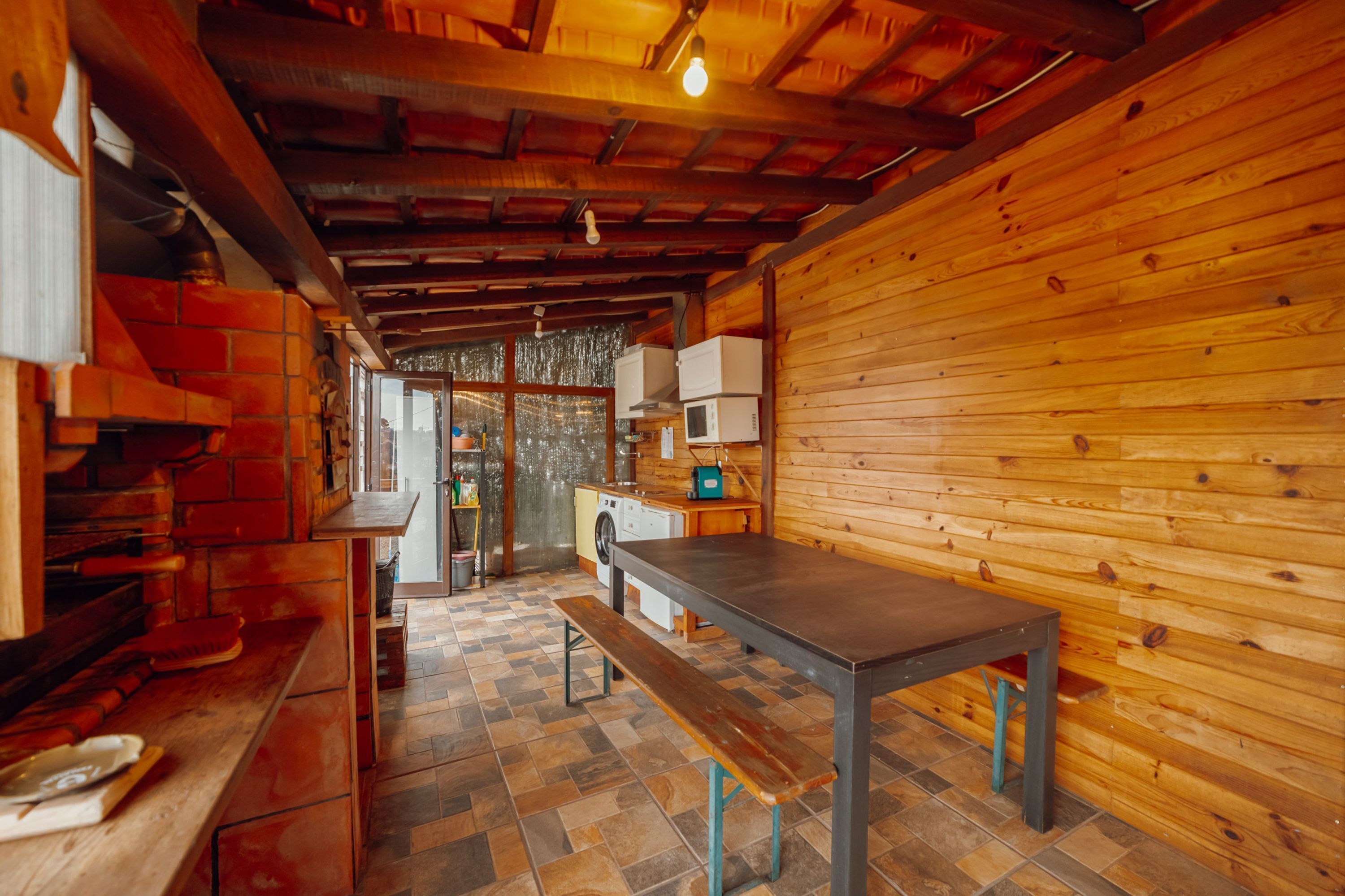 Uma cozinha rústica com interior de madeira, piso ladrilhado e um banco.