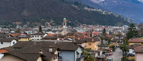 Uma cidade com uma torre do relógio imponente, rodeada por edifícios residenciais e ao fundo, montanhas.