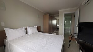 Quarto de hotel com cama grande, televisão, guarda-roupa e banheiro visível através de uma porta aberta.