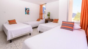 Quarto de hotel com três camas de solteiro, uma pequena mesa com uma planta e um quadro na parede.