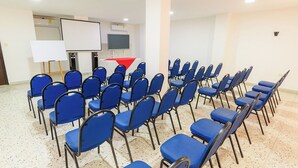 Uma sala de conferências com fileiras de cadeiras azuis, um quadro branco e uma tela de projeção.