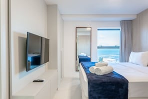Quarto de hotel com cama, televisão, espelho e vista para o mar.