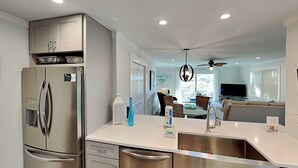 Cozinha moderna com eletrodomésticos de aço inoxidável, sala de jantar com cadeiras de vime e um ventilador de teto.