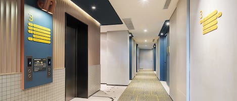 Corredor de hotel com um diretório digital, piso estampado e elevador moderno.