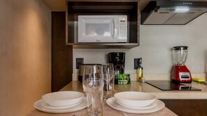 Cozinha equipada com micro-ondas, máquina de café, liquidificador e conjunto de jantar com pratos e copos.