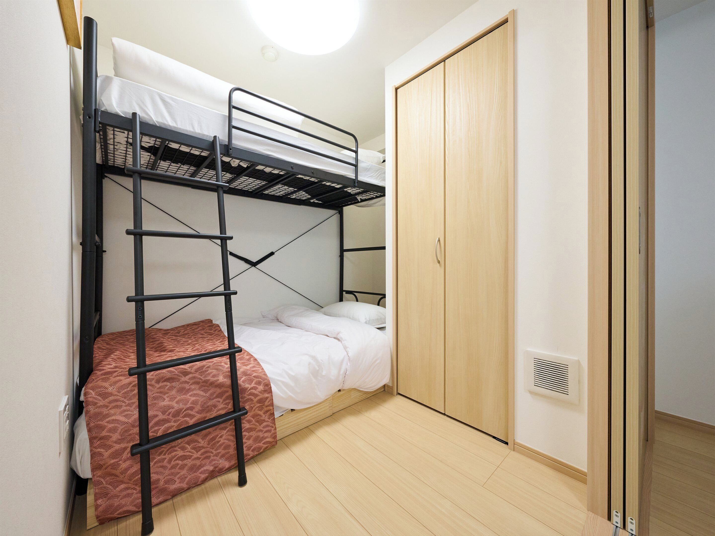 Uma cama beliche com escada, um guarda-roupa de madeira e uma parede branca.