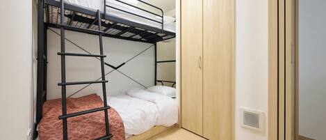 Uma cama beliche com escada, um guarda-roupa de madeira e uma parede branca.