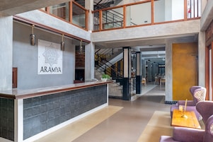 Uma mesa de recepção com uma placa indicando 'ARAMYA', uma escadaria e uma área de estar com uma mesa e cadeiras.