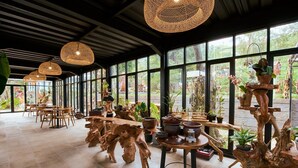 Um restaurante com grandes janelas, mesas de madeira e luminárias de vime suspensas.