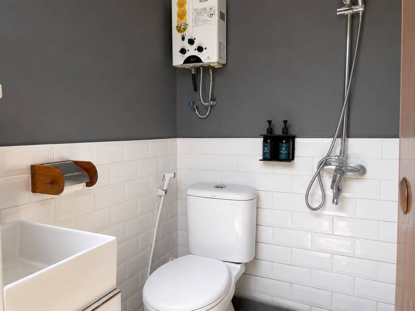Casa de banho com sanita branca, banheira branca, chuveiro com chuveiro manual e aquecedor fixado na parede.