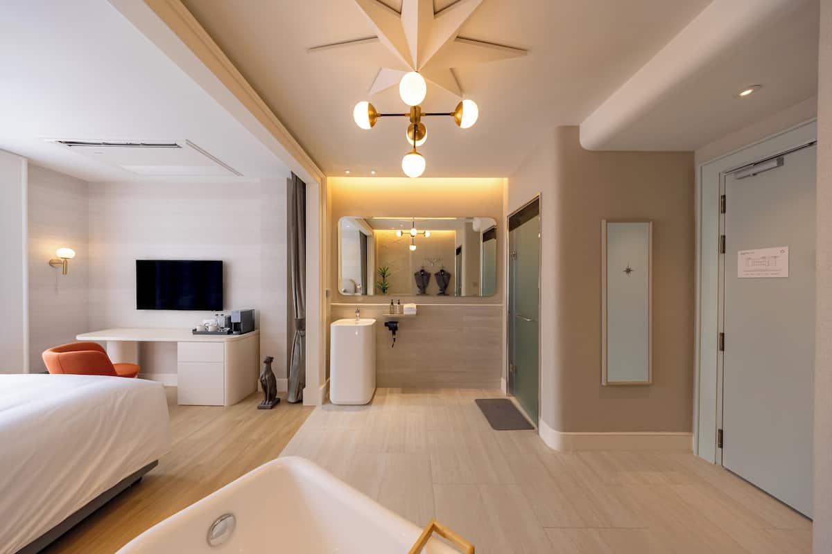 Quarto de hotel moderno com cama, escrivaninha, televisão, banheiro e um espelho grande.