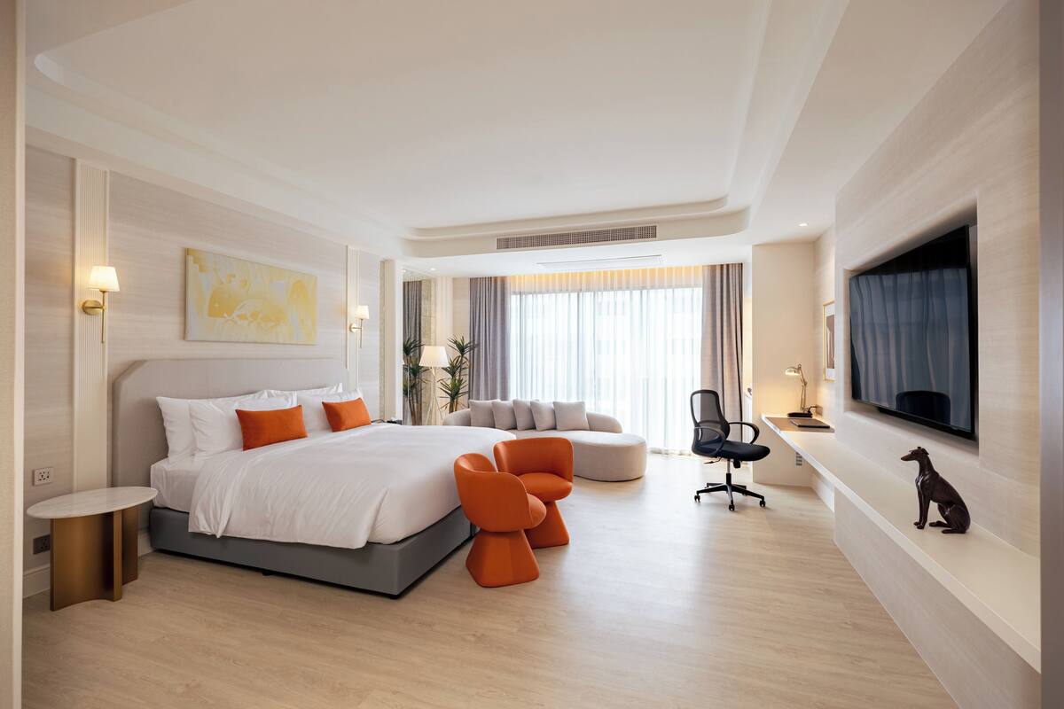Quarto de hotel moderno com uma cama grande, um sofá, uma escrivaninha e uma TV.