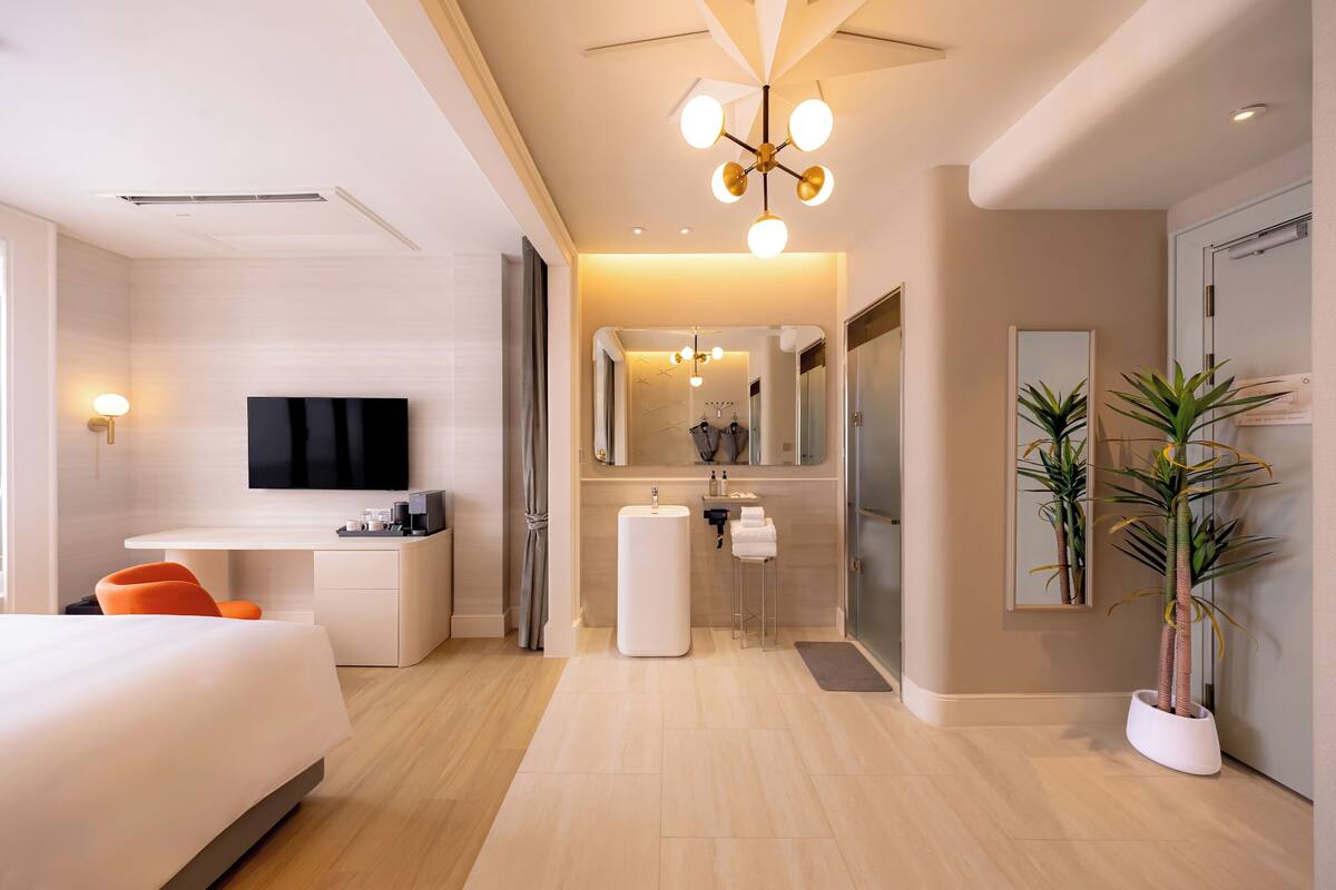 Quarto de hotel moderno com cama, escrivaninha, televisão, banheiro e um vaso de planta.