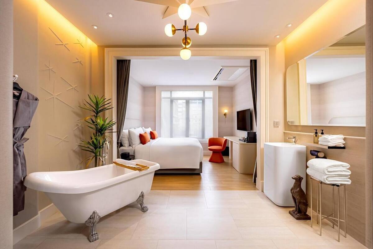Uma casa de banho de hotel moderna com uma banheira independente, um espelho grande e uma televisão de ecrã plano.