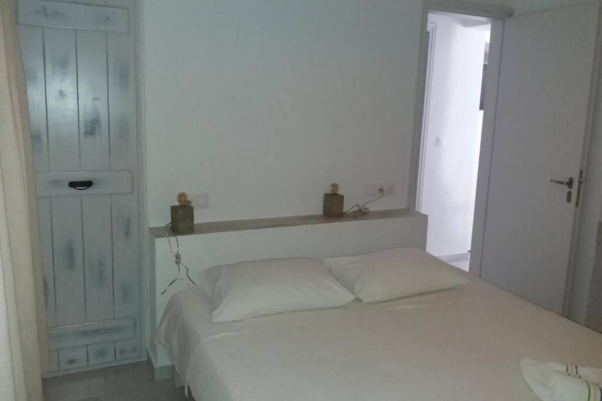 Um quarto com cama, guarda-roupa e porta que dá para outro cômodo.