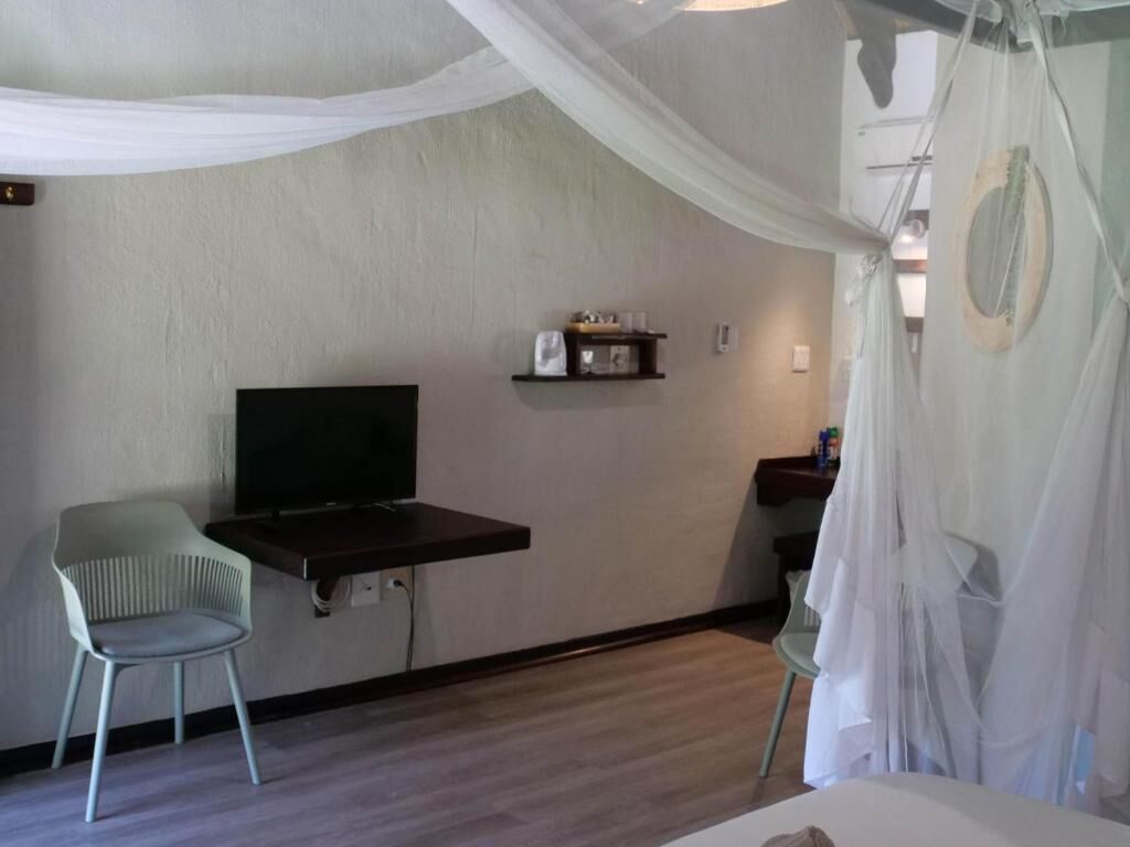 Um quarto com uma cama, uma televisão, uma escrivaninha e uma cadeira.