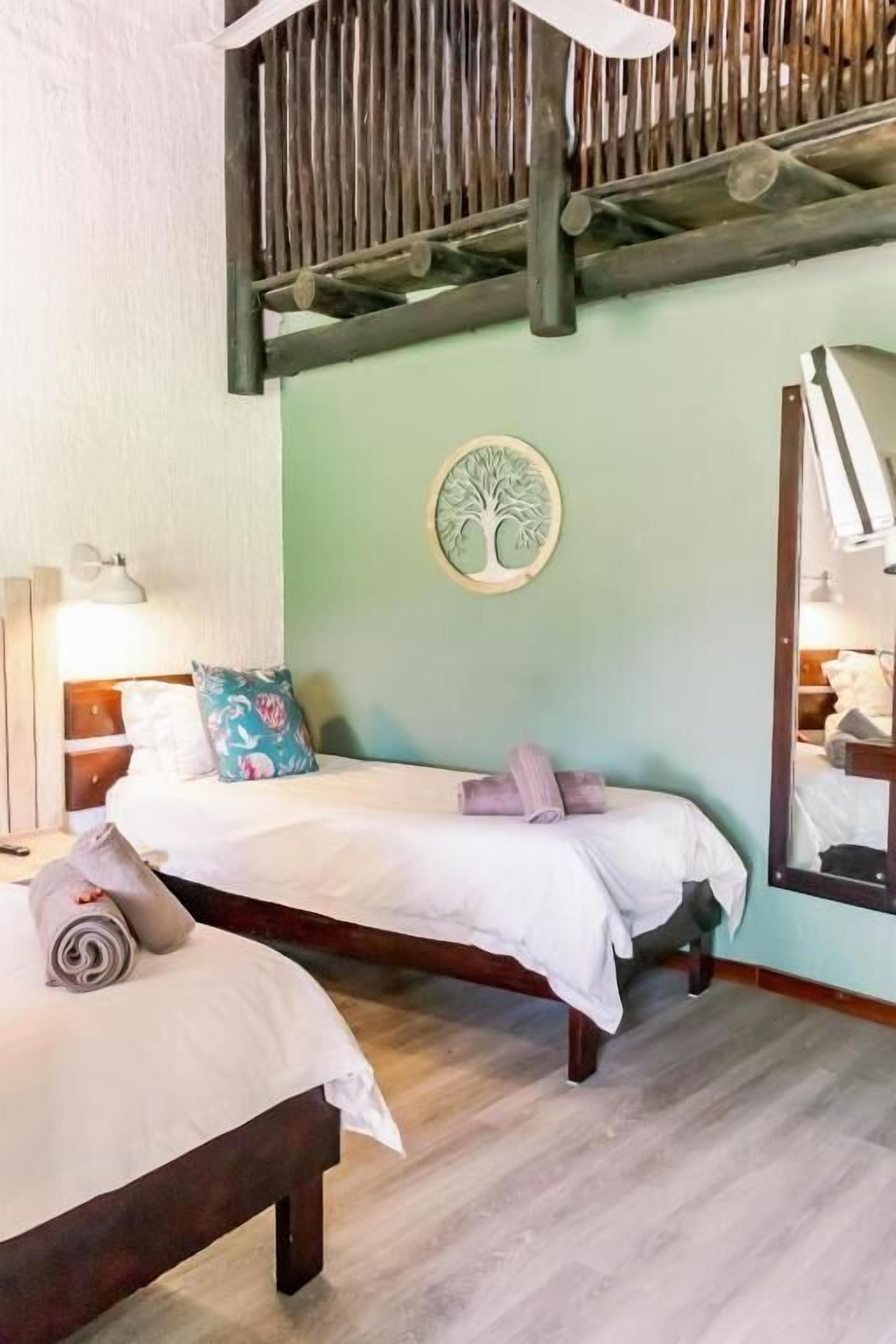 Quarto com duas camas, teto de madeira, decoração de árvore na parede e um espelho.