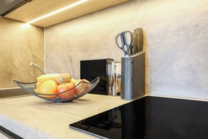 Uma bancada de cozinha com uma fruteira contendo bananas, laranjas e maçãs, um bloco de facas e um eletrodoméstico preto.