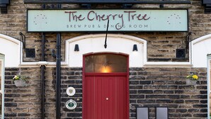 Um edifício de tijolos com uma porta vermelha, uma placa com a inscrição 'The Cherry Tree Brew Pub & Dining Room' e uma janela acima da porta.