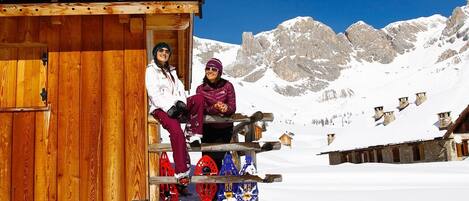Uma cabana de madeira com varanda, rodeada por montanhas cobertas de neve.