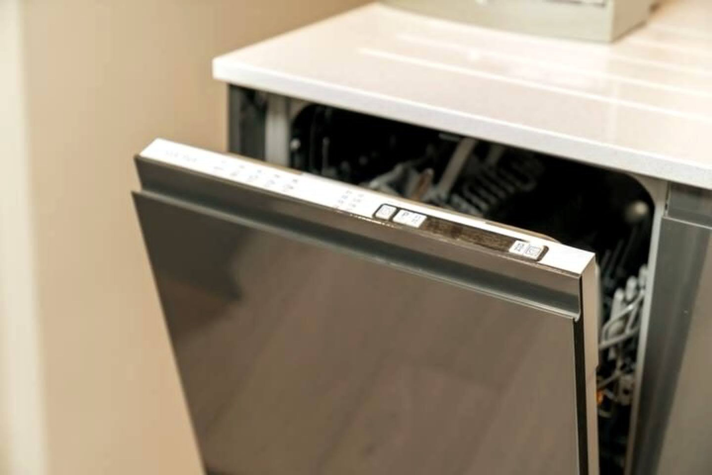 Uma máquina de lavar loiça moderna com painel de comando, numa cozinha com bancada branca.
