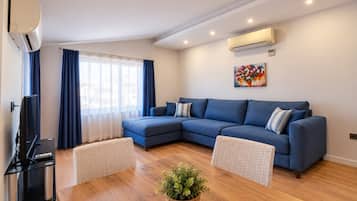 Uma sala de estar moderna com um sofá seccional, uma TV de tela plana, uma mesa de jantar de madeira e uma planta em vaso.