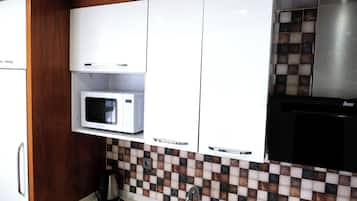 Cozinha com armários brancos, micro-ondas, chaleira e painel de azulejos.