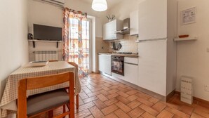 Cozinha compacta com mesa de jantar, televisão e luminária pendente.