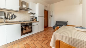 Cozinha compacta com armários brancos, fogão, forno e área de refeições com mesa e cadeiras.