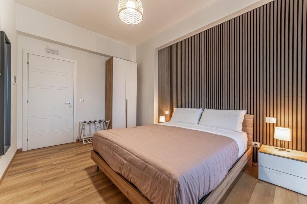 Quarto moderno com uma cama grande, cabeceira de ripas de madeira, mesa de cabeceira com abajur e um guarda-roupa.