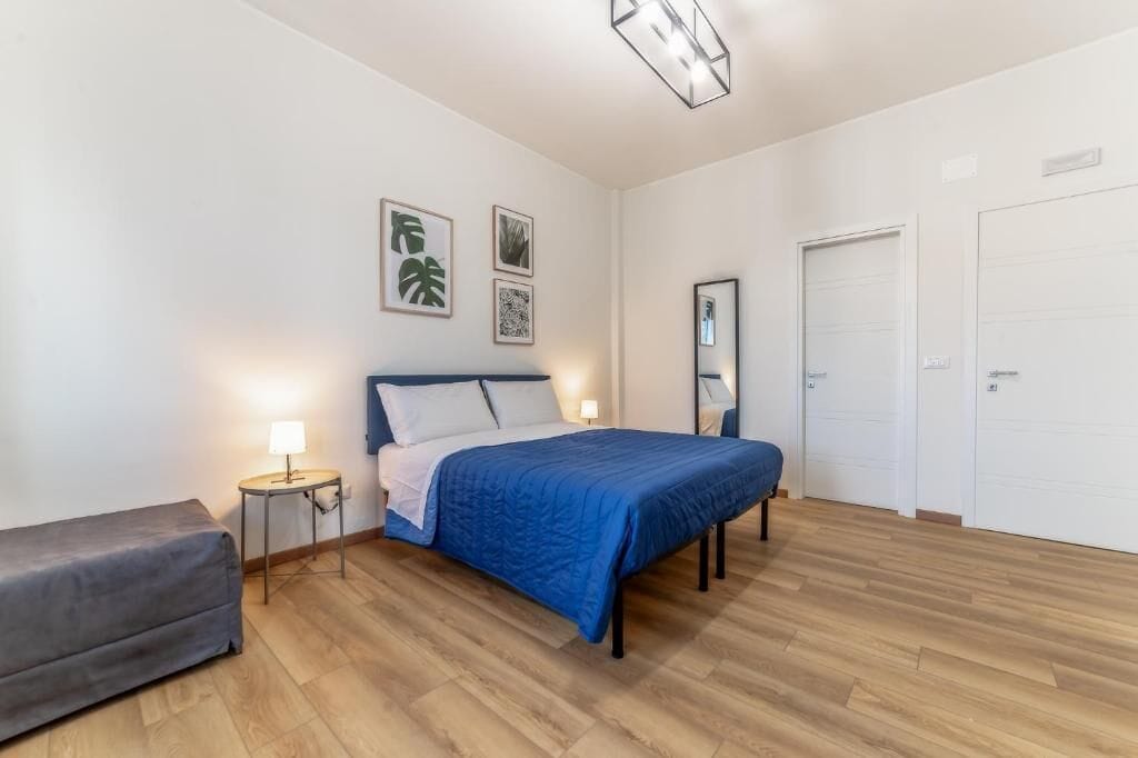 Quarto com cama, mesas de cabeceira, um banco, um espelho e uma porta.