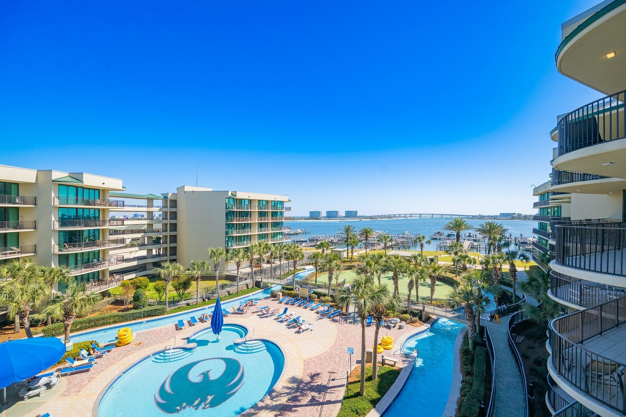 Um hotel com piscina, palmeiras e vista para o oceano.