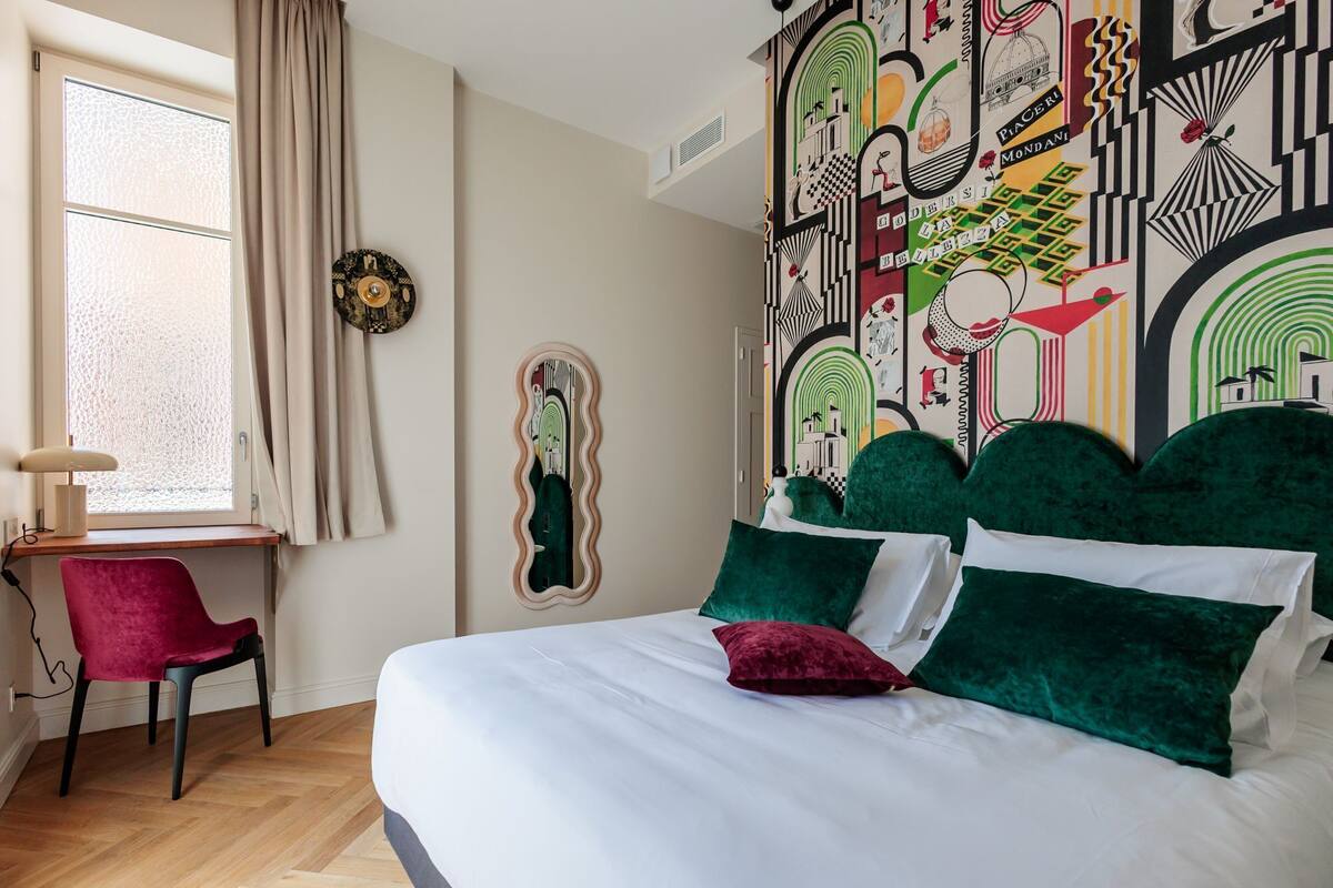 Quarto com cama, escrivaninha, cadeira e uma grande obra de arte abstrata na parede.