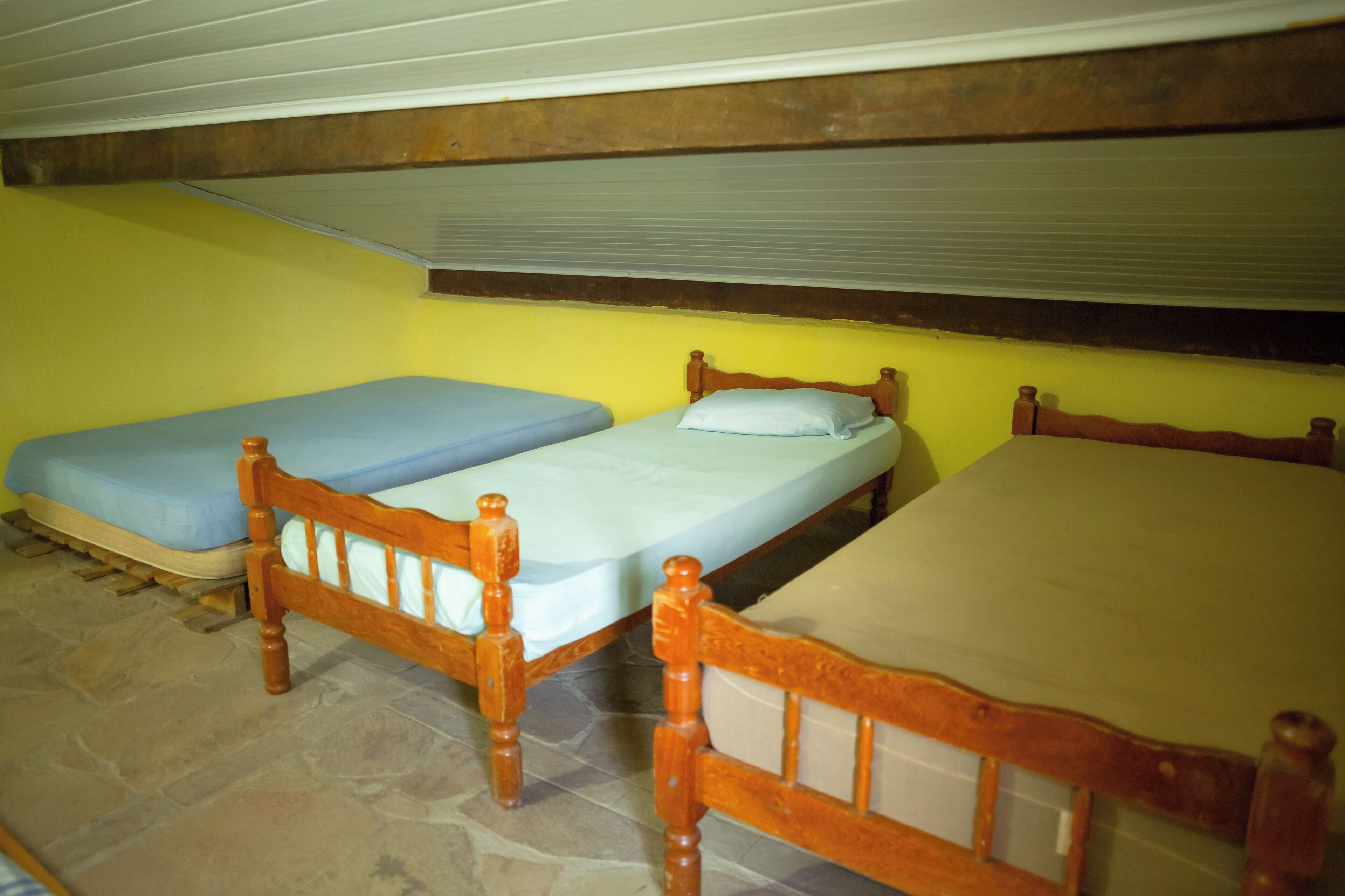 Quarto com duas camas de madeira, parede amarela e teto inclinado.