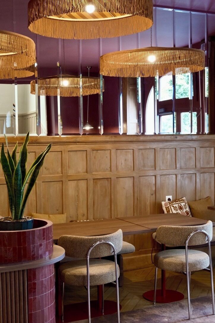 Interior de restaurante com parede de painéis de madeira, mesas redondas e cadeiras de metal.