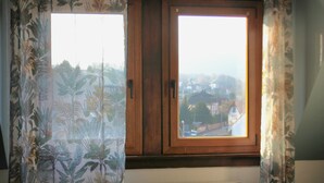 Uma janela com vista para uma cidade, cortinas com padrão de folhas e moldura de madeira.