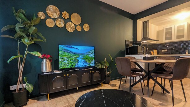 Uma sala de estar moderna com televisão de tela plana, uma área de refeições com cadeiras, uma mesa de centro de mármore preto e arte decorativa na parede.