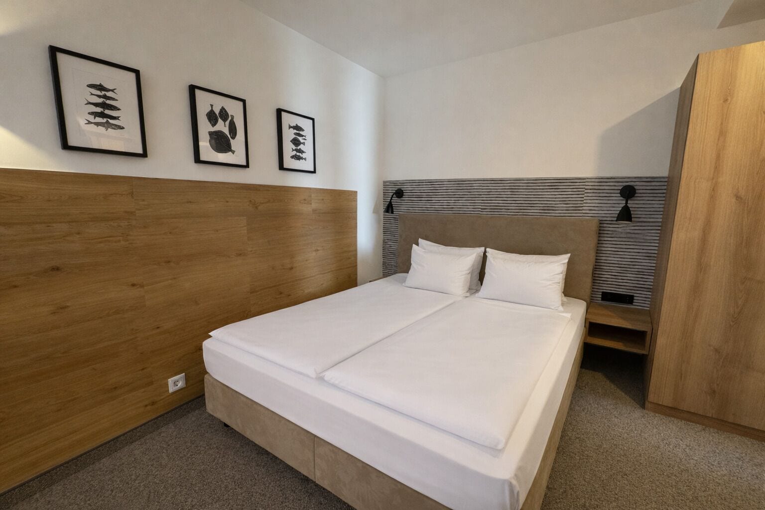 Uma cama de casal com lençóis brancos, uma cabeceira de madeira e três quadros na parede.