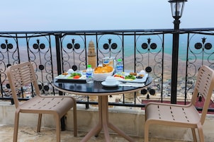 Varanda com mesa posta para refeição, duas cadeiras, um abajur e vista para um edifício distante.