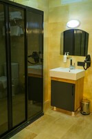 Casa de banho com chuveiro em cabine de vidro, lavatório com espelho em cima e sanita visível através do vidro.