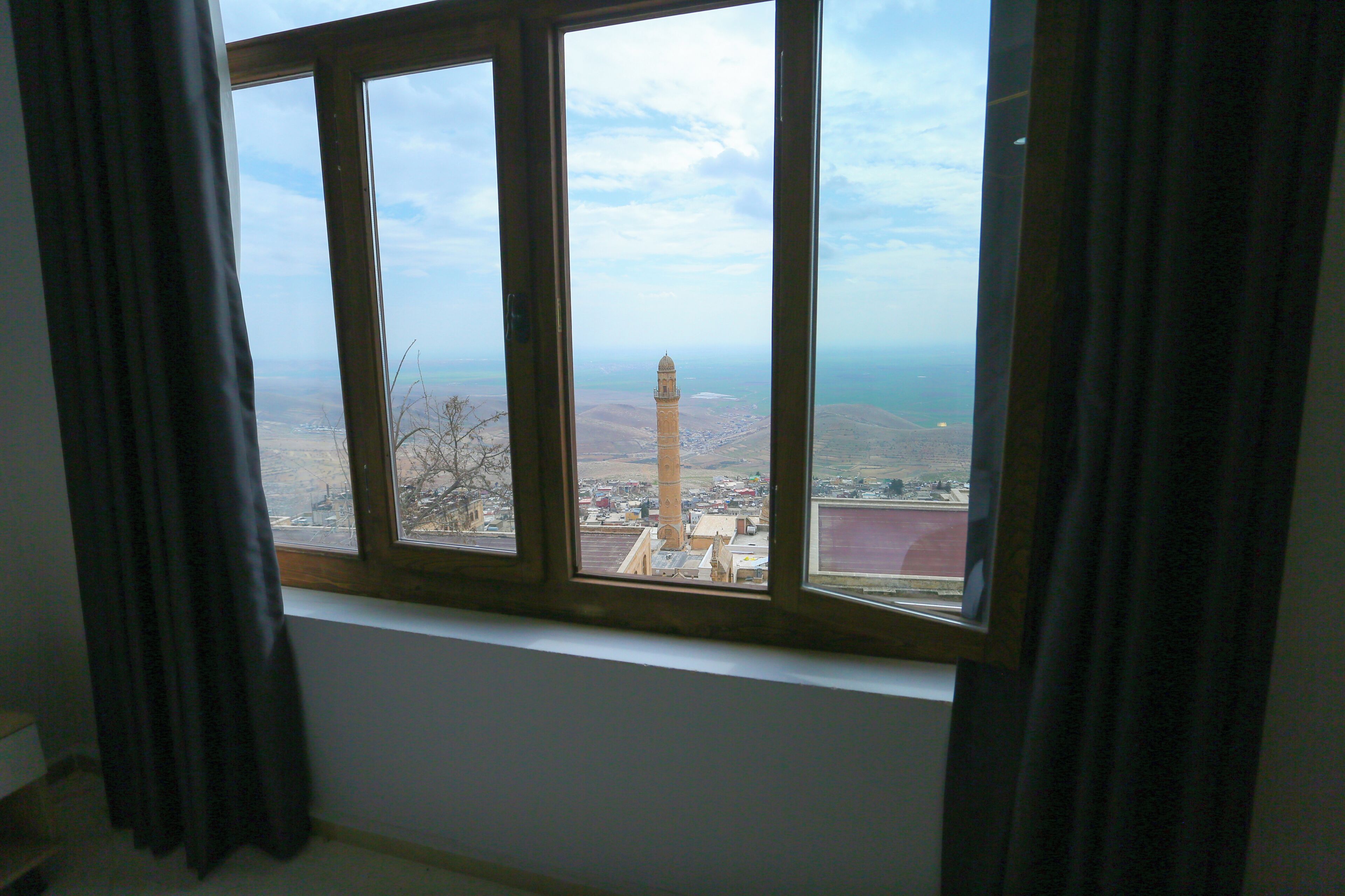 Janela com vista para uma paisagem distante, incluindo uma torre e um corpo de água.