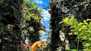 Um jardim com uma grande escultura de serpente, rodeado por folhagem densa e plantas tropicais.