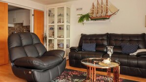 Uma sala de estar com um sofá de couro preto, uma poltrona reclinável, uma mesa de centro de vidro e um modelo de navio na parede.